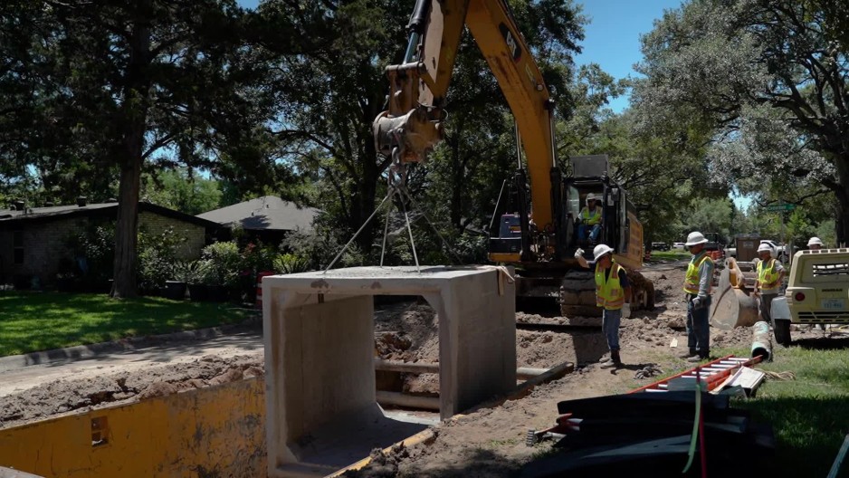 Construction excavator lowering concrete pipe precast into hole on ...