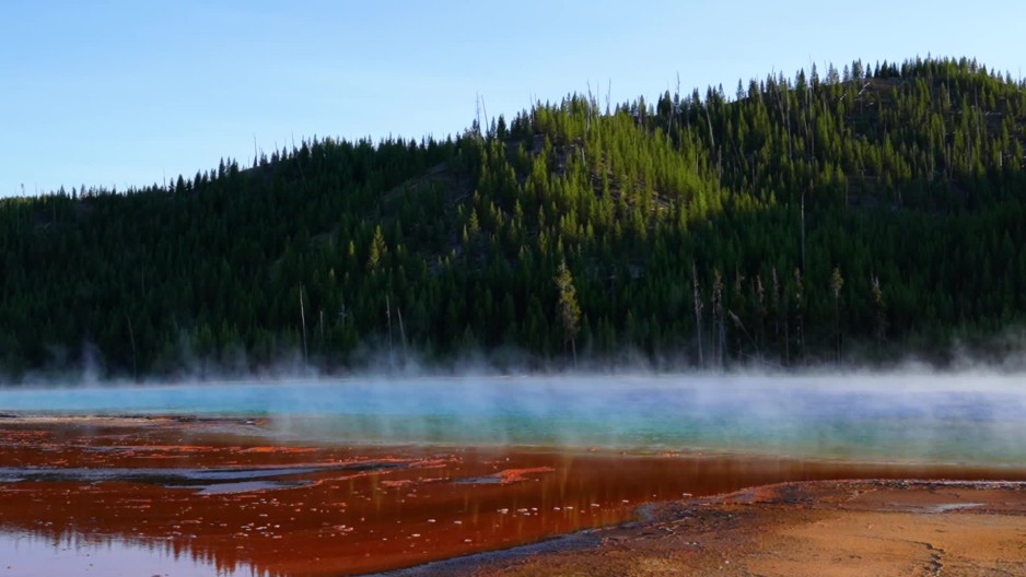 Water vapor emitting off colorful hot spring with forest background ...