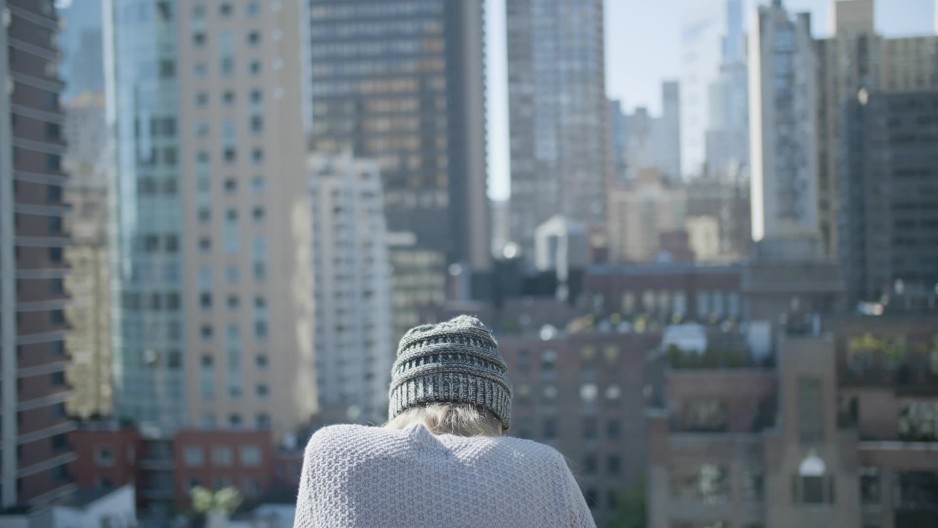 Young woman standing on rooftop balcony in New York City looking over ...