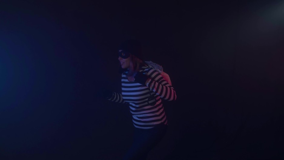 Cute female dressed up in robber costume tip toeing with bag of money ...