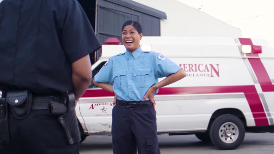 Female EMT laughing with hands on hips while talking with cop outside ...