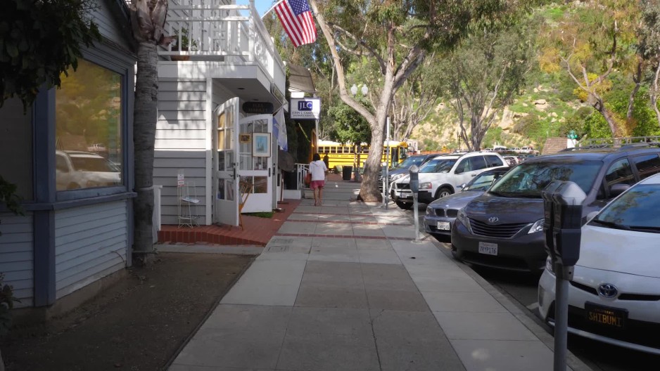 Wide tilt up of woman walking along storefront sidewalk in Laguna Beach ...