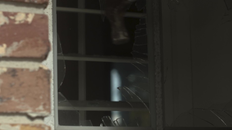 Burglar breaking window pane by front door with a hammer and reaching ...