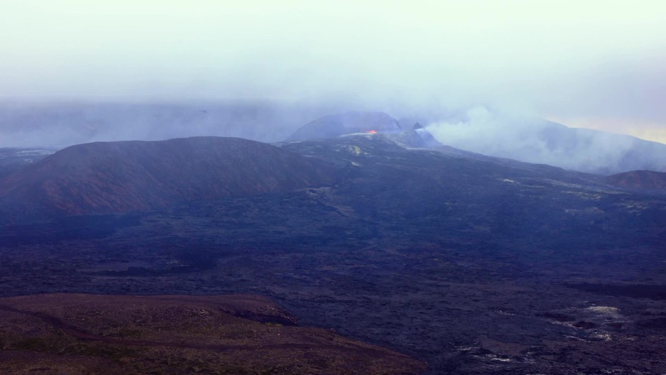 Volcanic field covering hills with active volcano in background | ClipStock