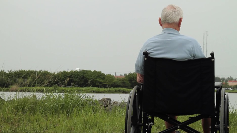 Hovering behind elderly man in wheelchair near lake | ClipStock