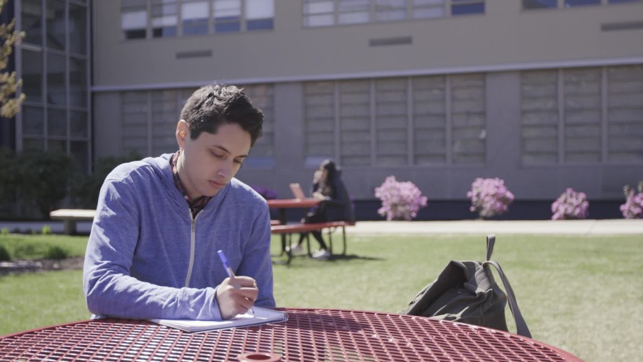 Mid of student writing in notebook at table on campus | ClipStock