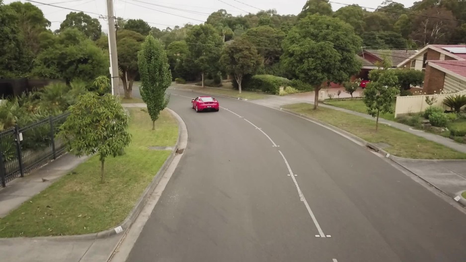 Red luxury sports car driving around corner on empty residential street ...