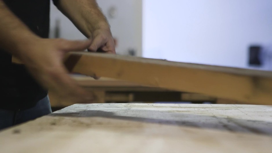 Man pulling wood plank onto workbench | ClipStock