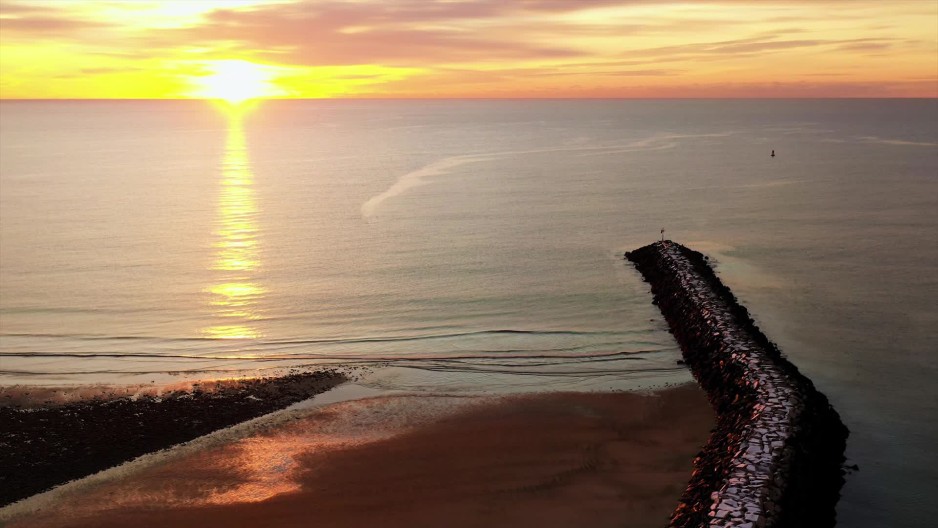 Sun reflecting off ocean at sunset near land bank | ClipStock