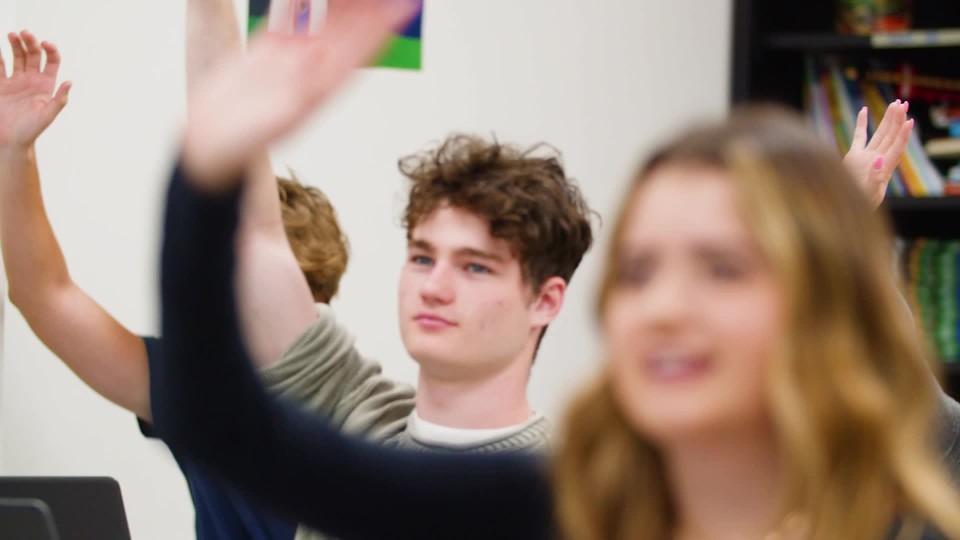 Students sitting in high school classroom lowering raised hands | ClipStock