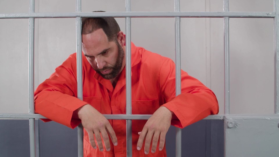Vengeful male criminal in prison cell turning towards camera | ClipStock