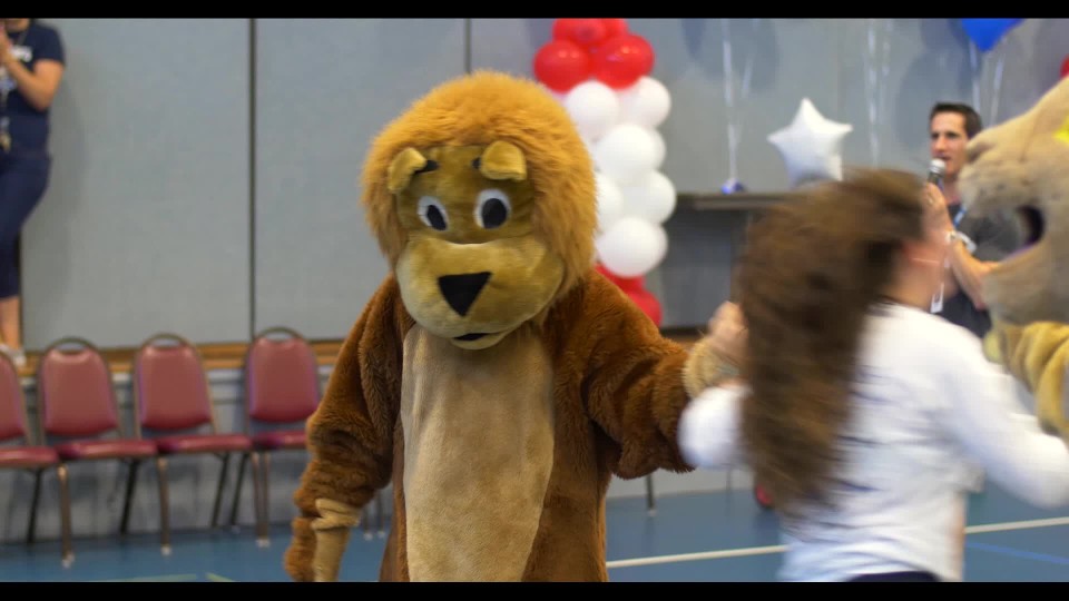 Male coach with microphone explains rules to ball relay game inside ...